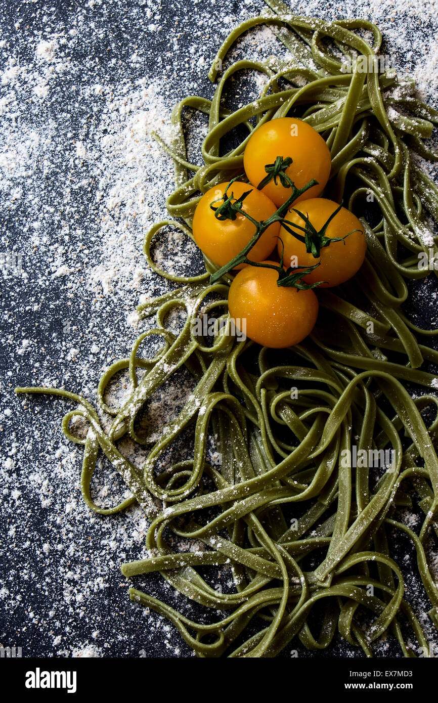 Raw homemade pasta with tomatoes and flour over dark gray background ...