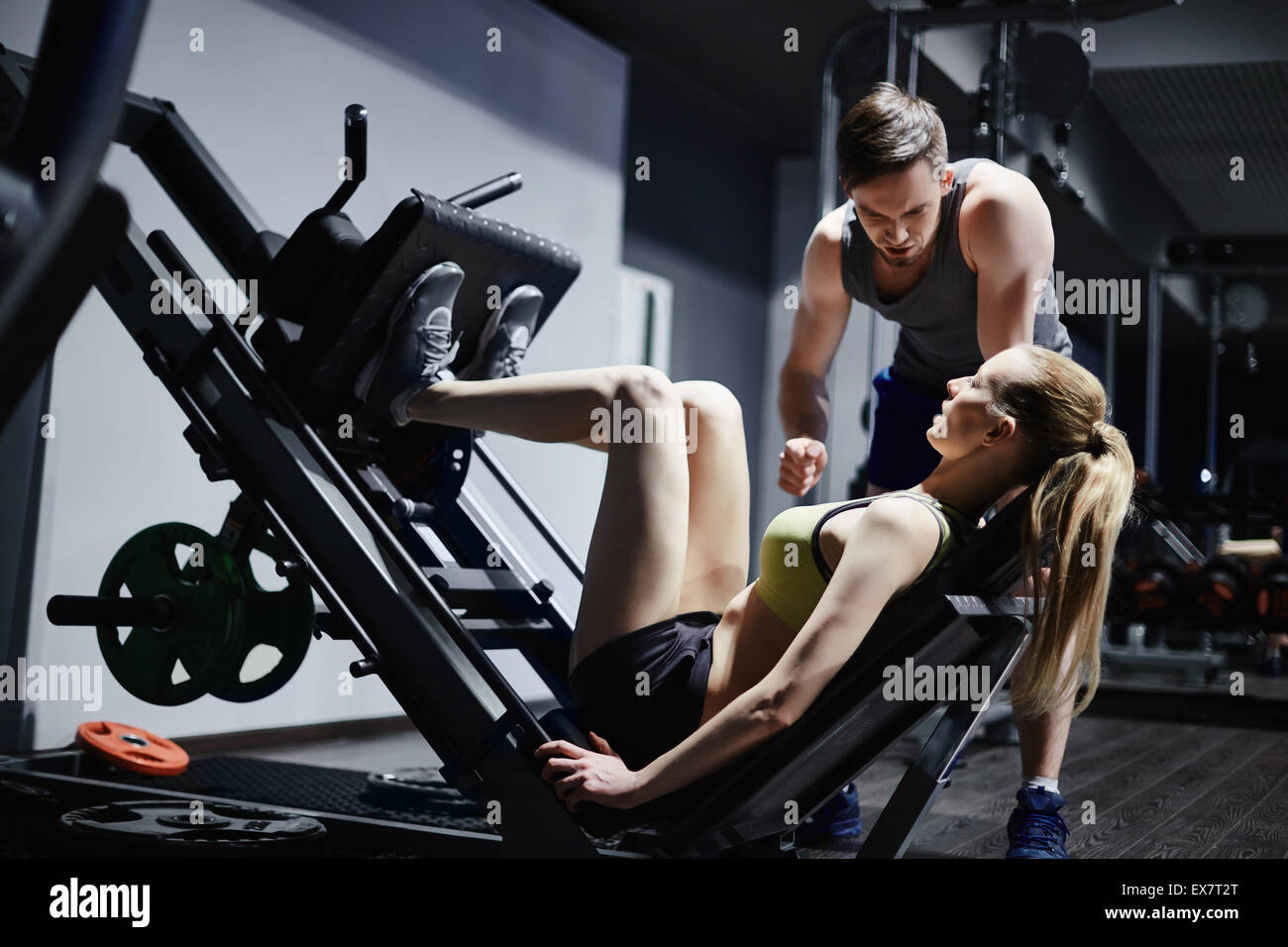 Attractive girl strengthening leg muscles on facilities while trainer ...