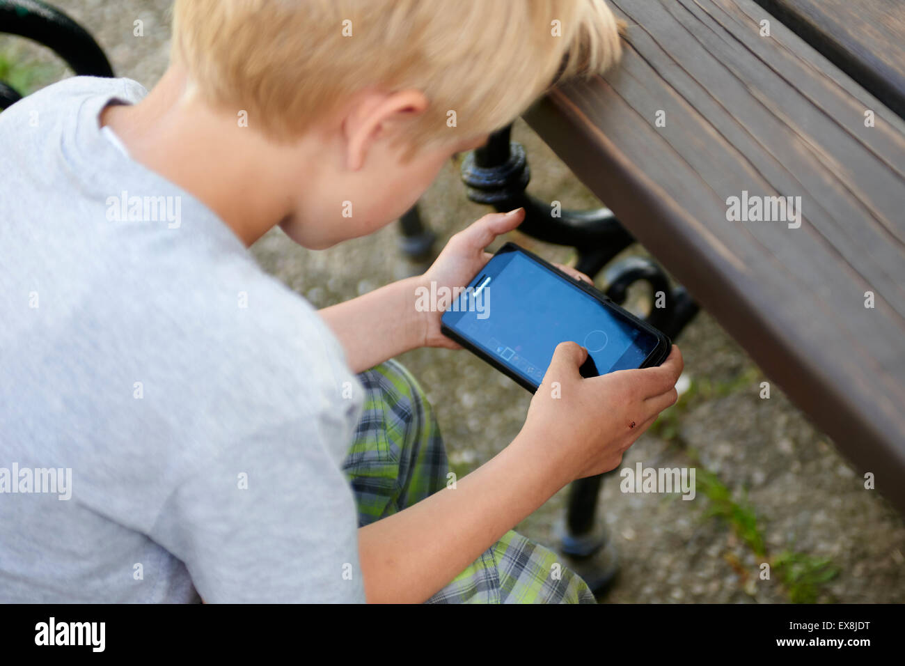 Child blond Boy sitting on a garden bench using a mobile (cell) smart ...