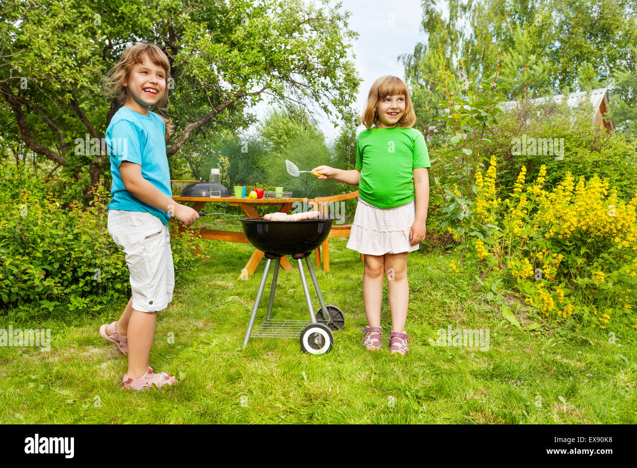 Two small sisters standing near BBQ and grilling Stock Photo - Alamy