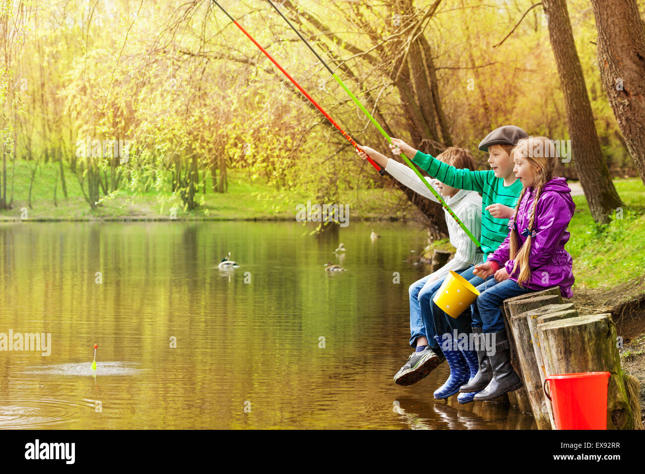 Happy friends sit fishing together near pond Stock Photo - Alamy