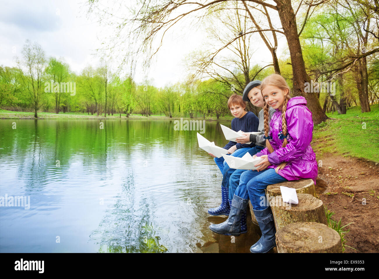 Smiling friends hold paper boats near river Stock Photo - Alamy