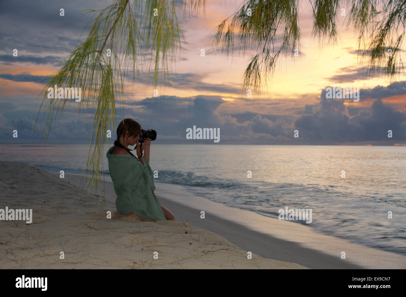 A young woman sits on the sandy shores of the Indian Ocean and taking ...
