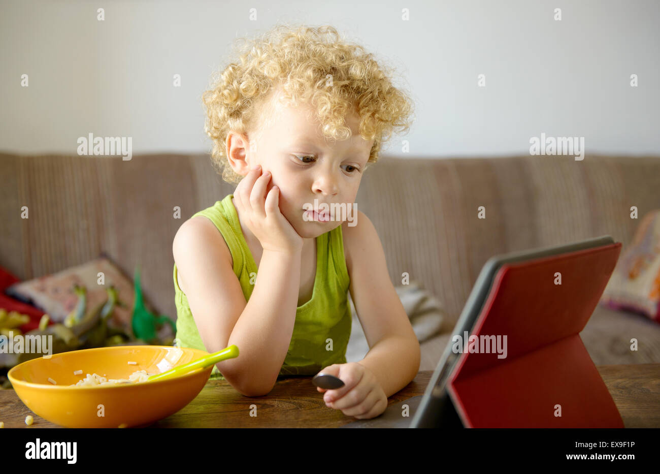 a little child looking at a digital tablet and eating Stock Photo - Alamy