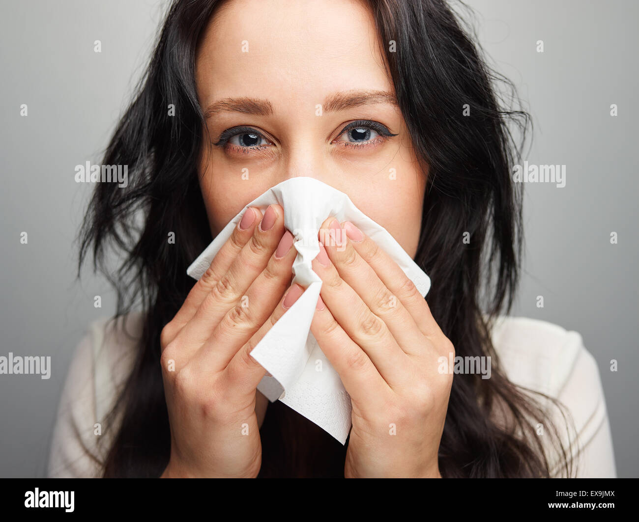 Close up, young woman blowing her nose, gray background Stock Photo - Alamy