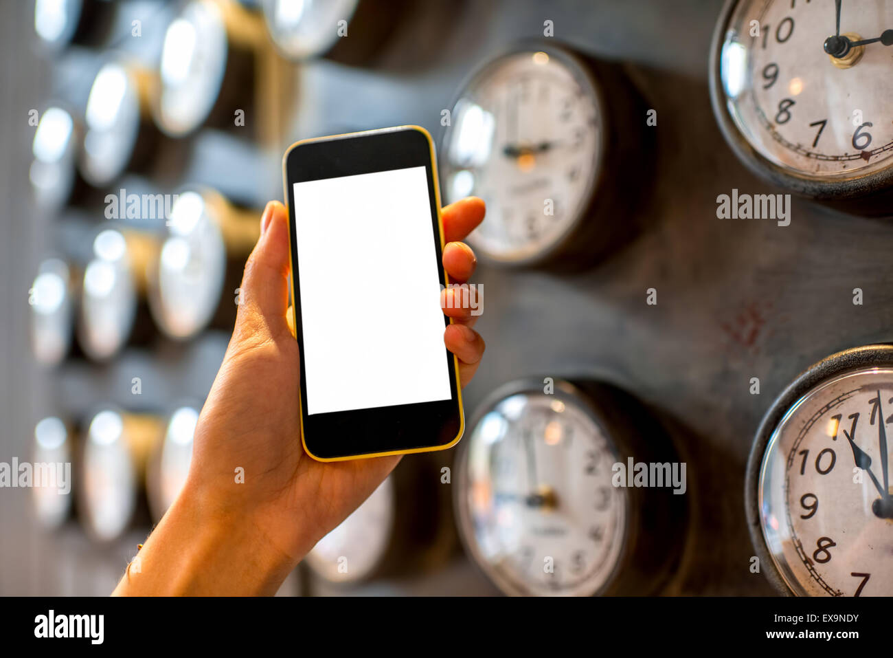 Female hand holding phone with white screen and metal clocks on ...