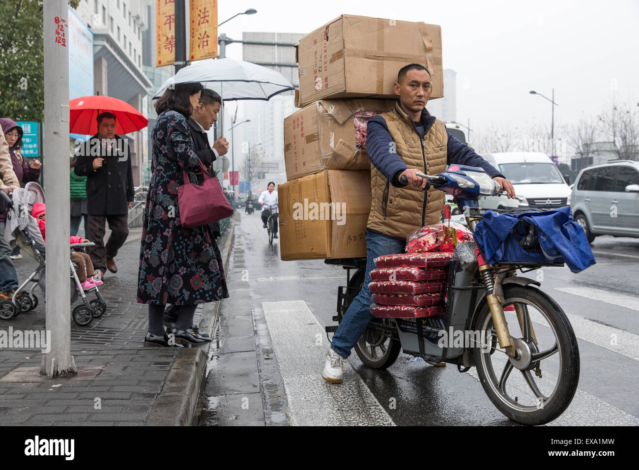 China, Shanghai, Man riding motorcycle overloaded with boxes stands at ...