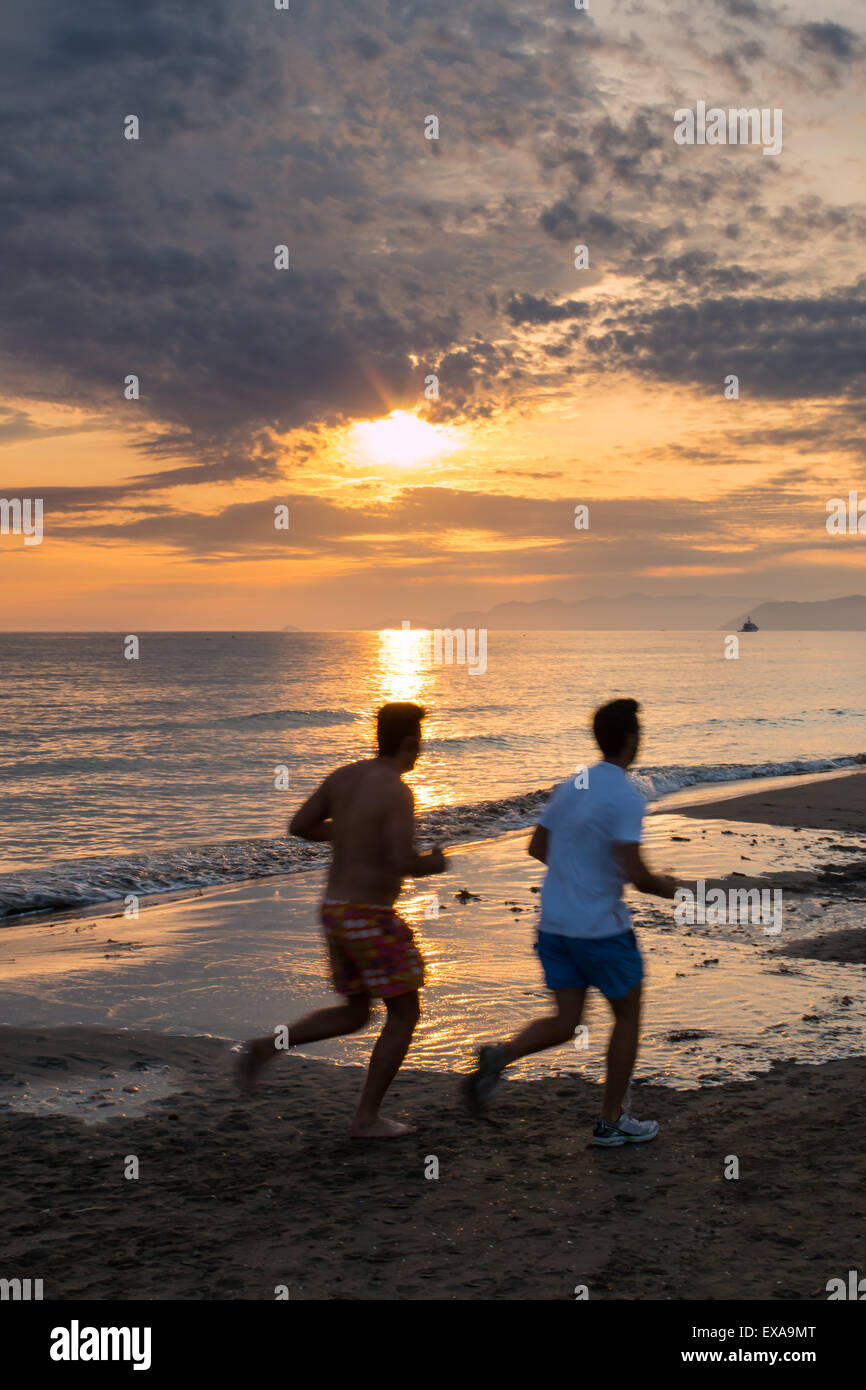 Two guys running on the beach at sunset in a cloudy evening Stock Photo ...