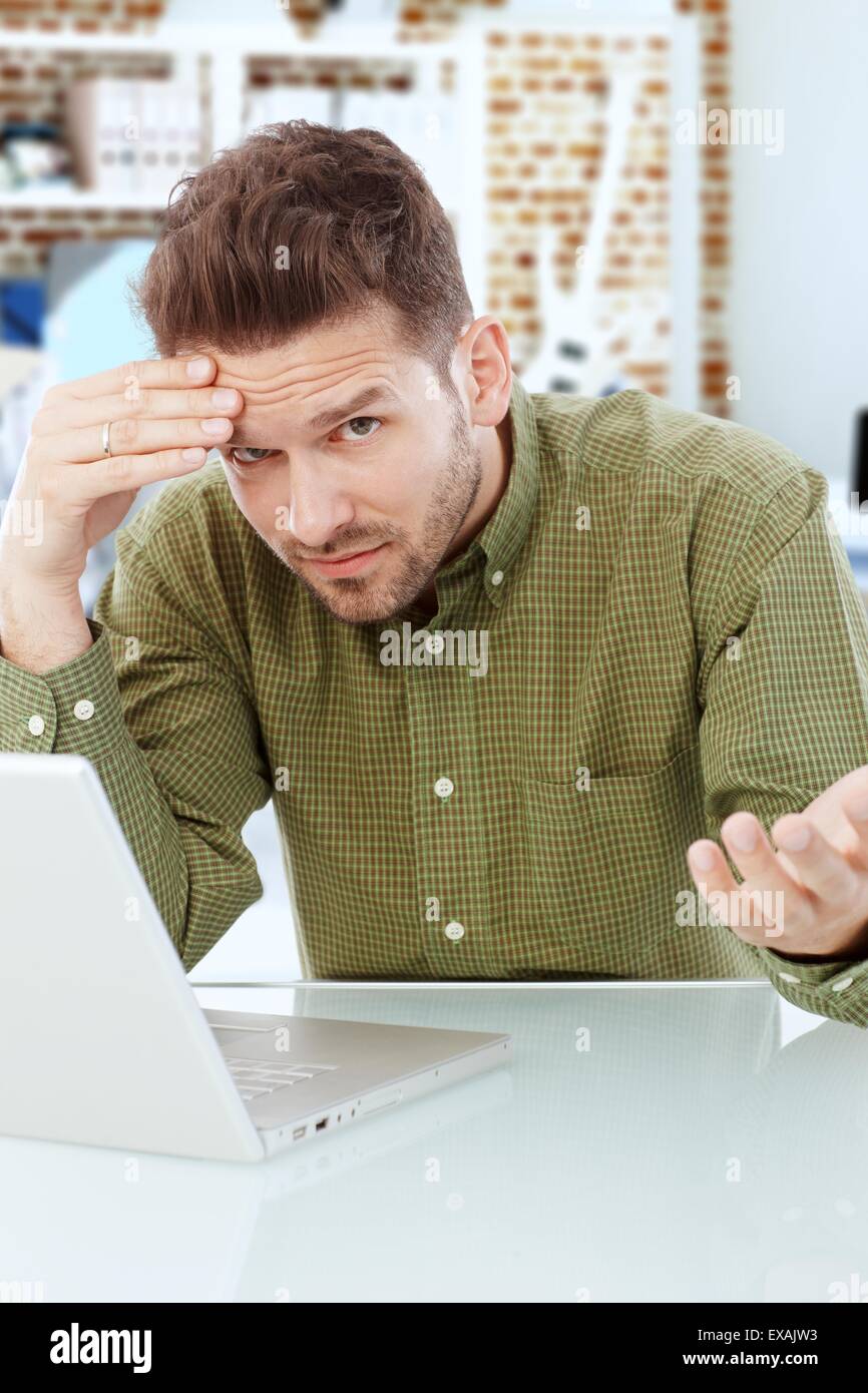 Young man sitting at desk, using laptop, looking desperate Stock Photo ...