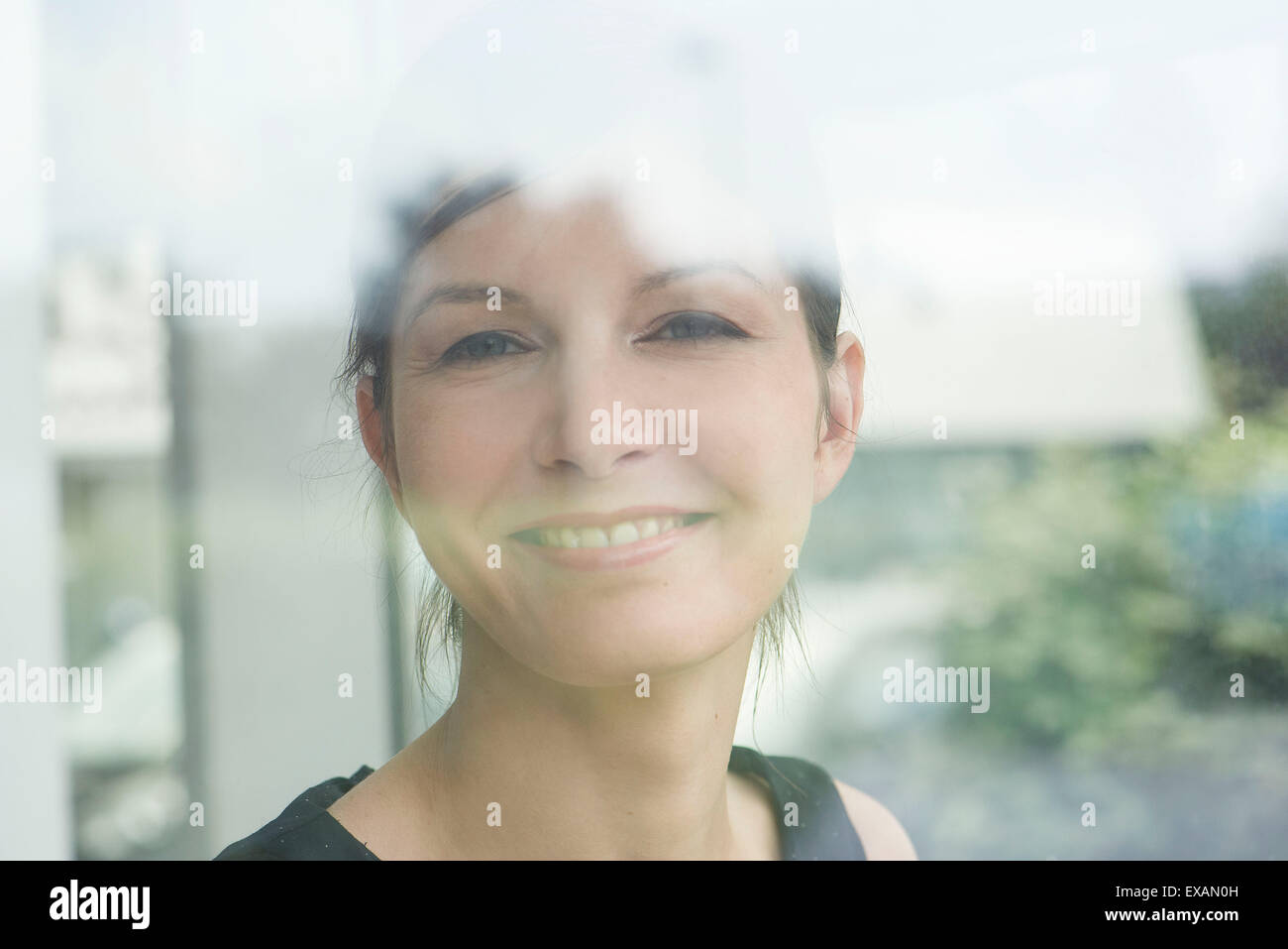 Woman looking through window, smiling, portrait Stock Photo - Alamy