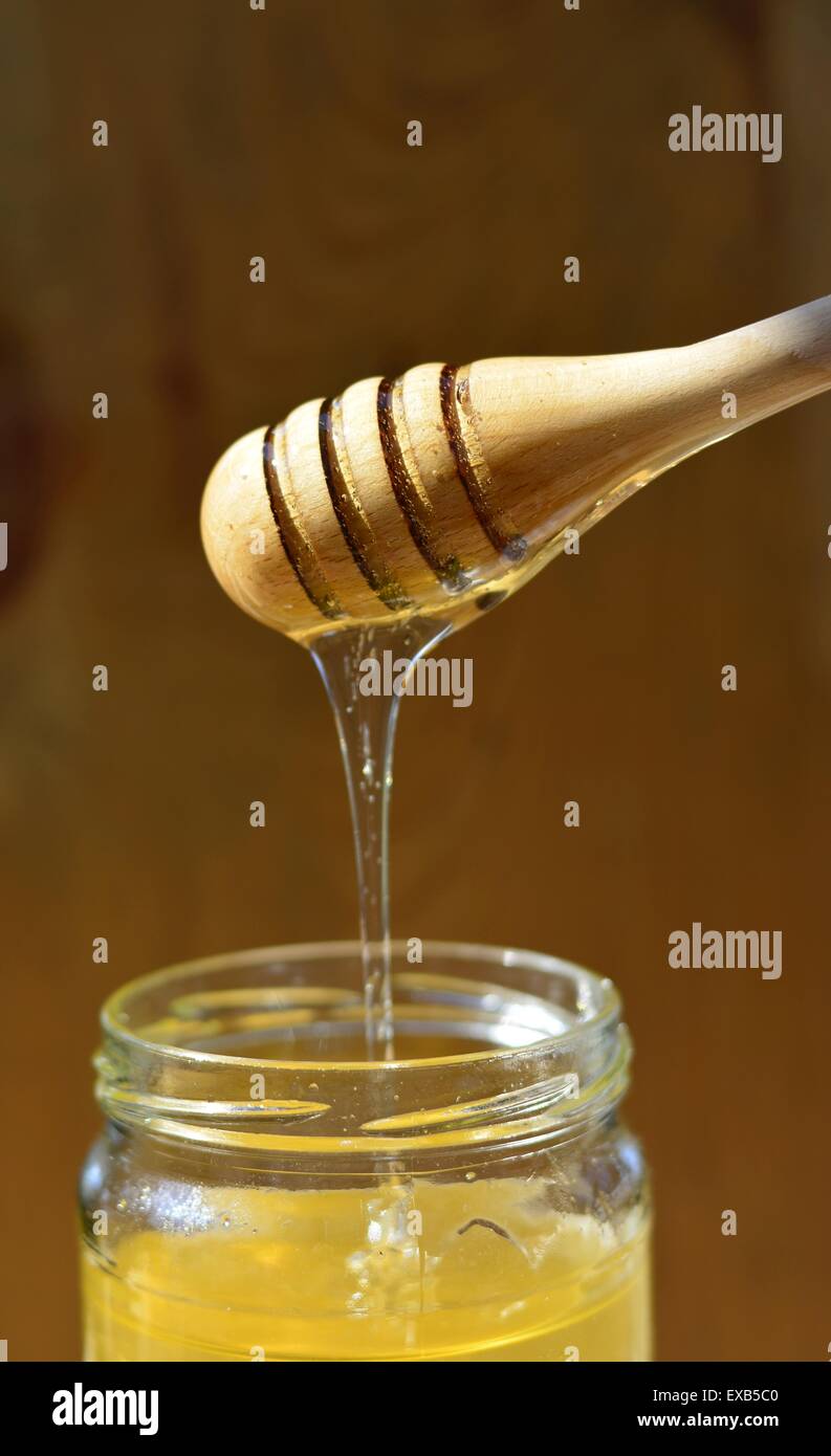 Honey pouring from stick to the jar Stock Photo - Alamy