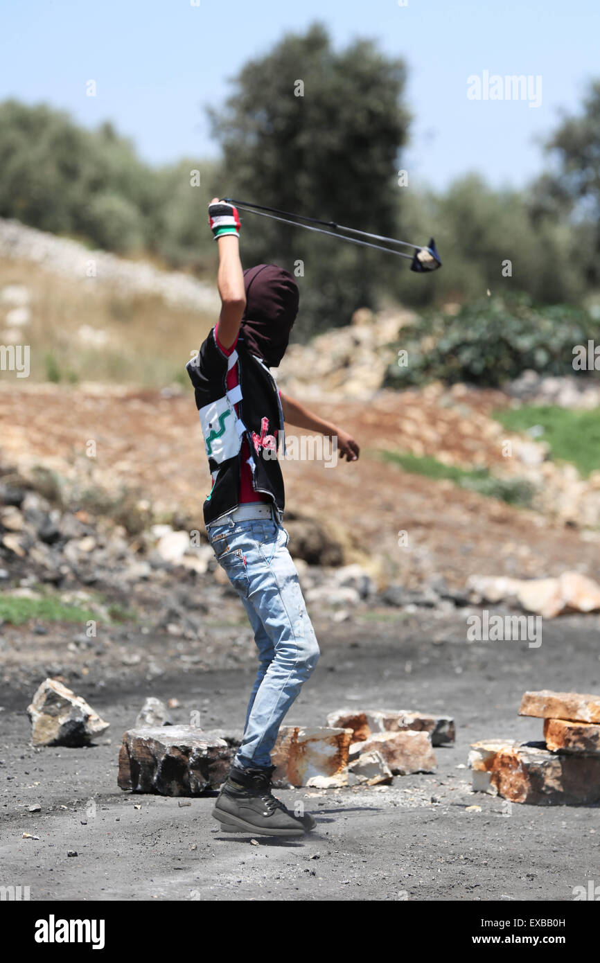 A masked Palestinian youth hurls a rock at Israeli troops stationed on ...