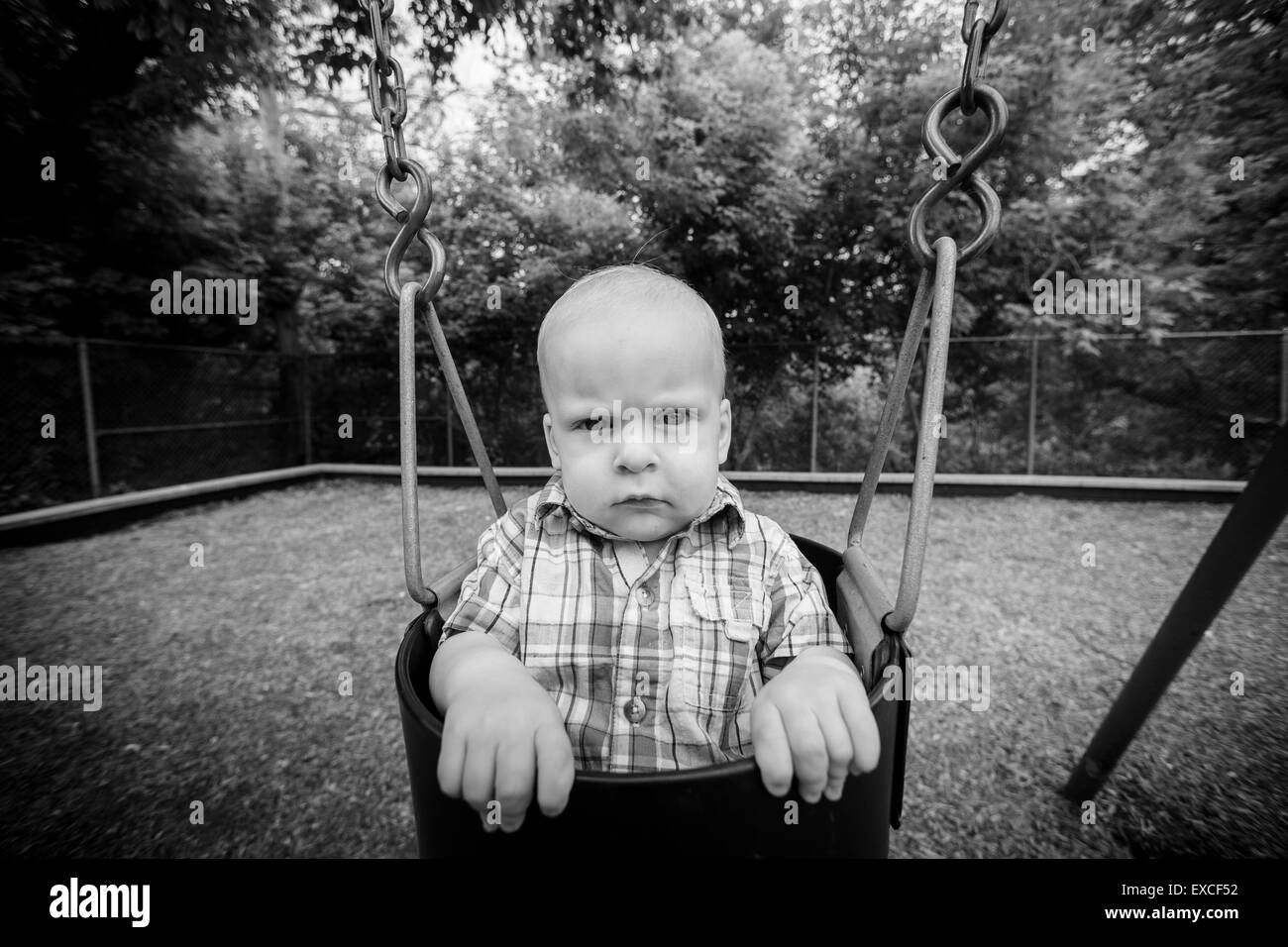 A toddler with a serious face sits in a swing at a playground Stock ...