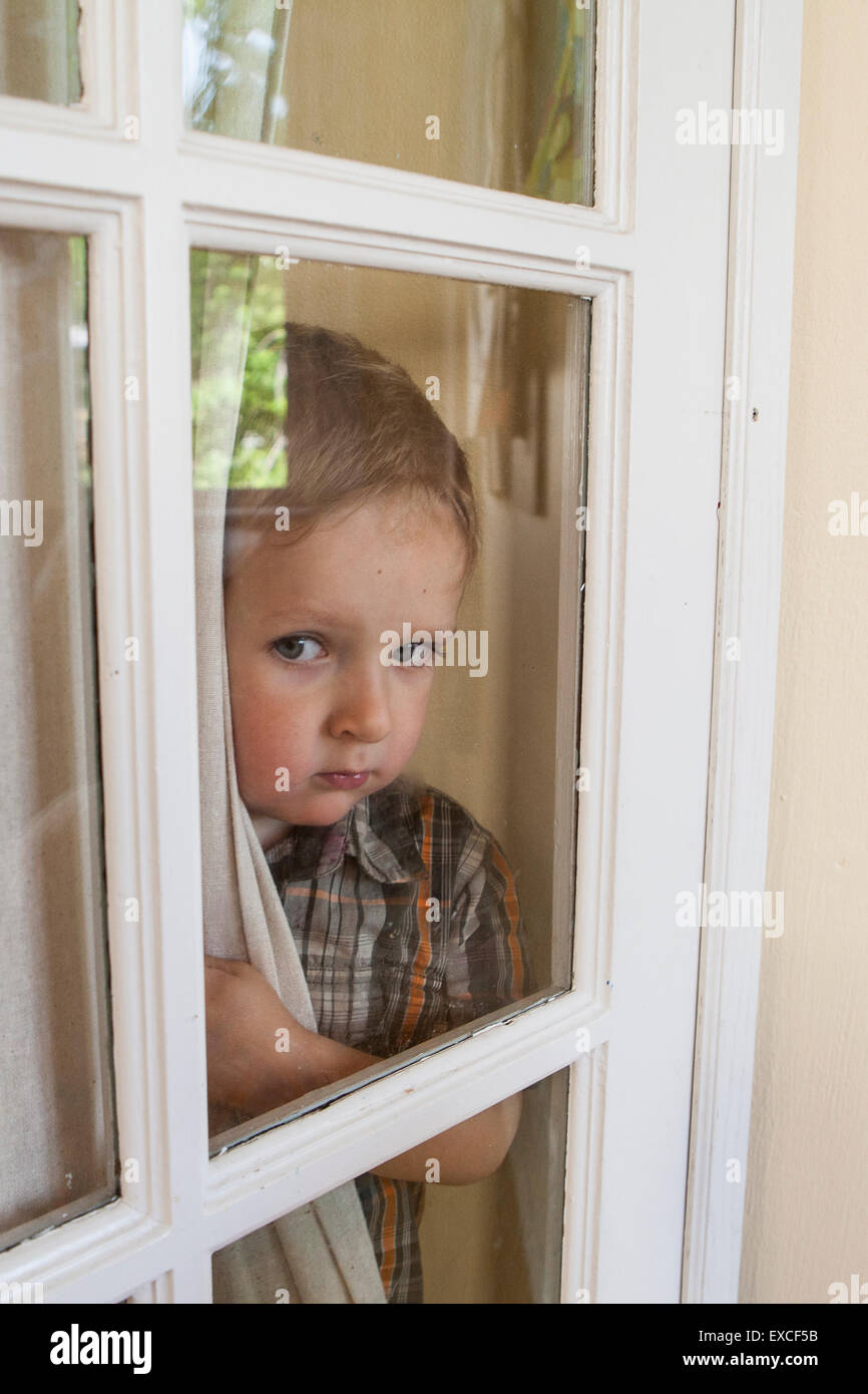 A young boy peeks out of the window pane of a door Stock Photo - Alamy