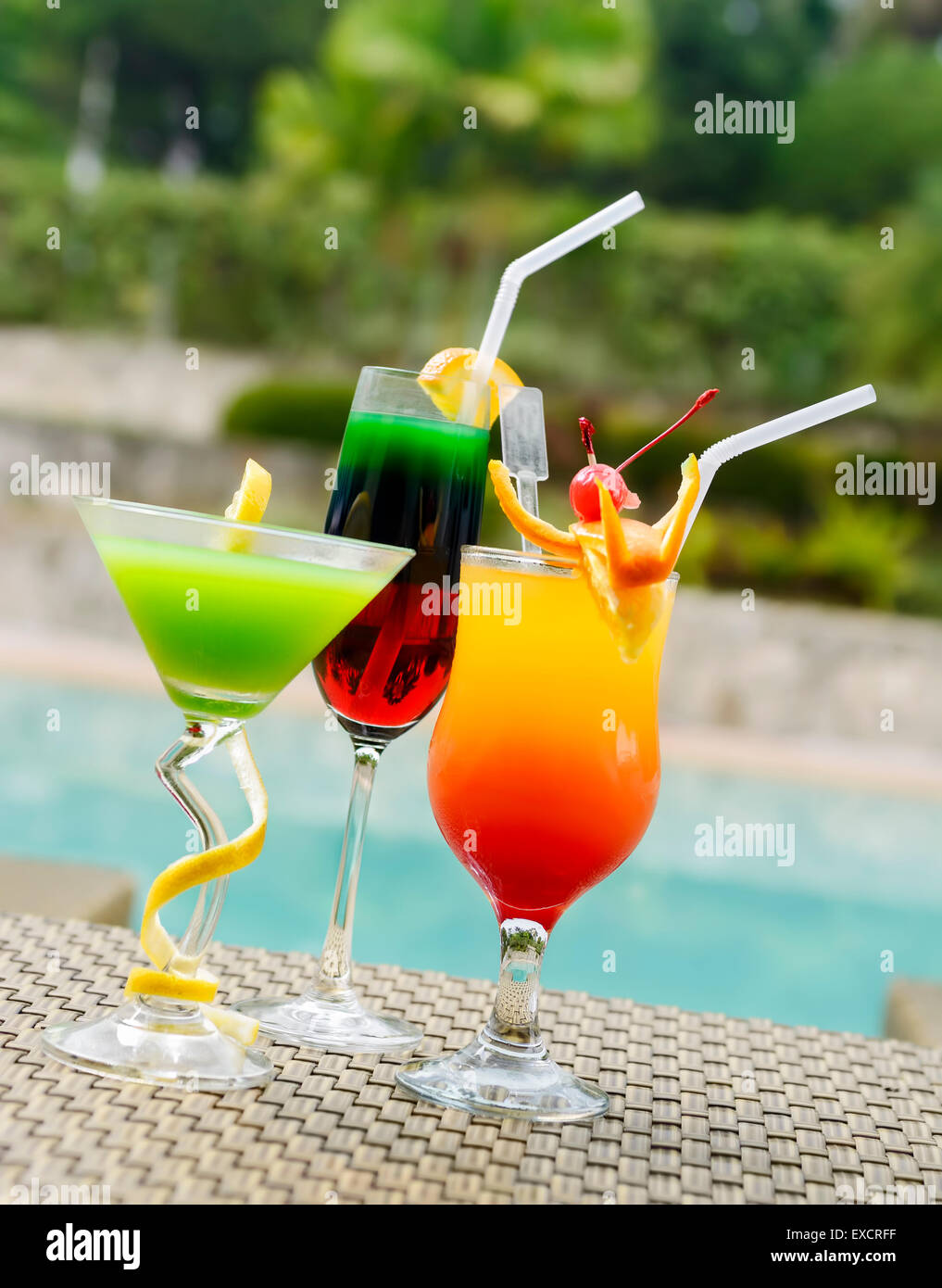 Multicolor tropical pool cocktails on table in front of swimming pool ...