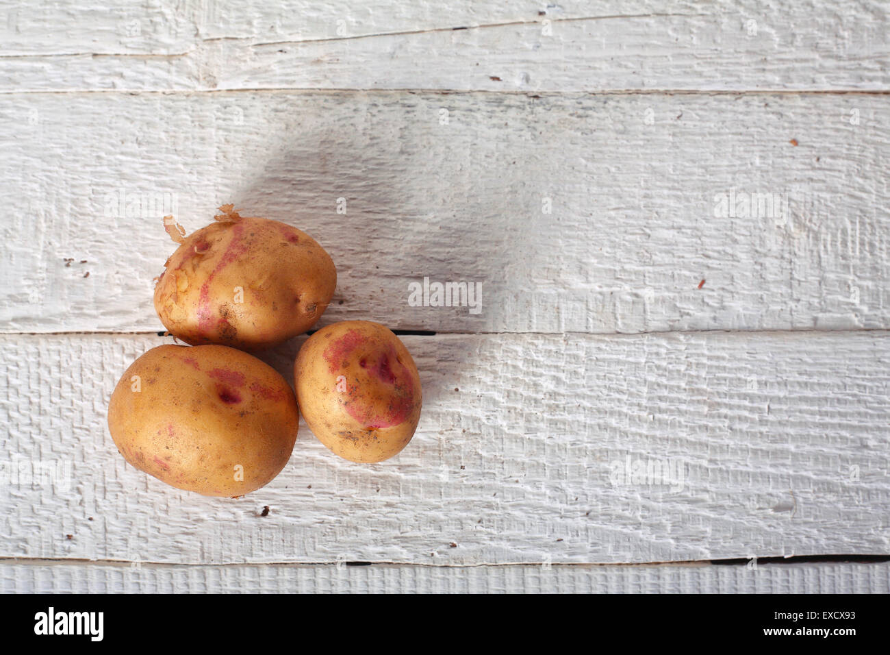 Three potatoes on old white planks a background Stock Photo - Alamy