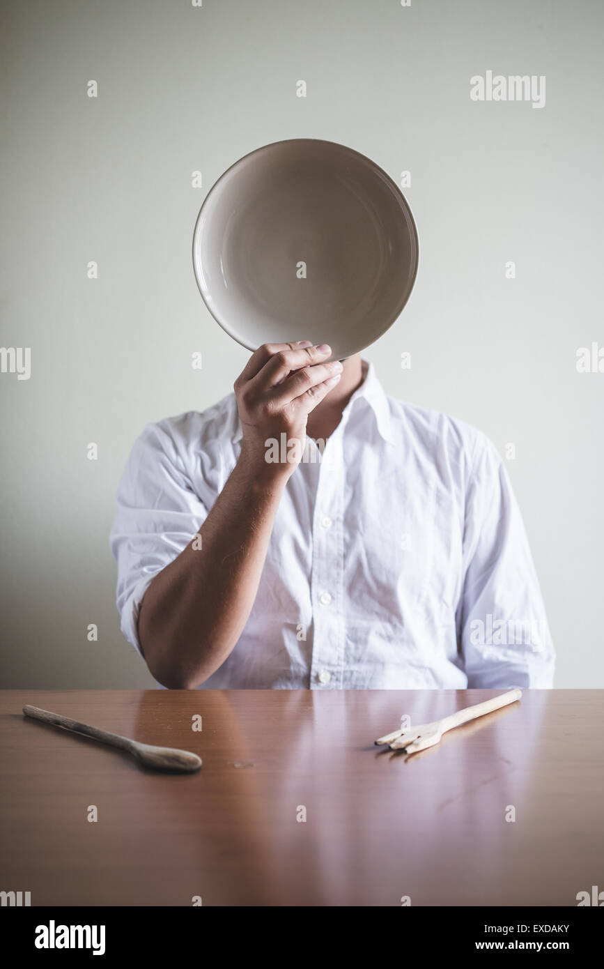 young stylish man with white shirt and dish in his face behind a table ...