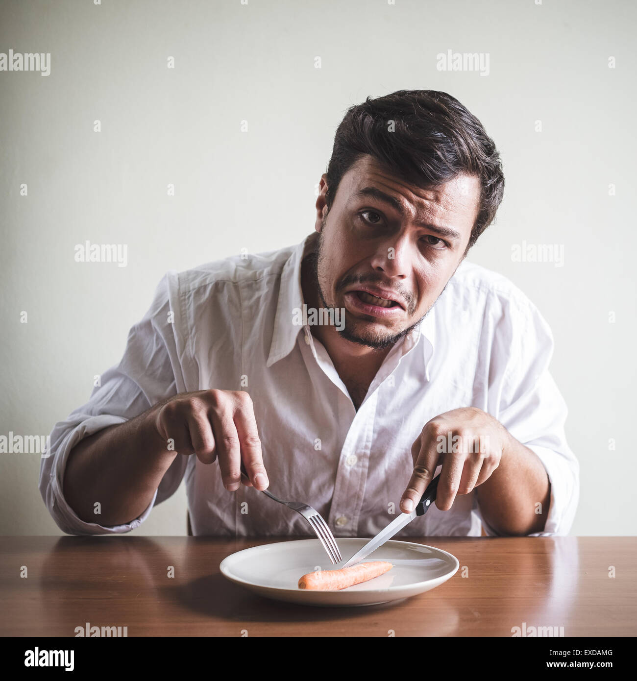 young stylish man with white shirt eating carrot behind a table Stock ...