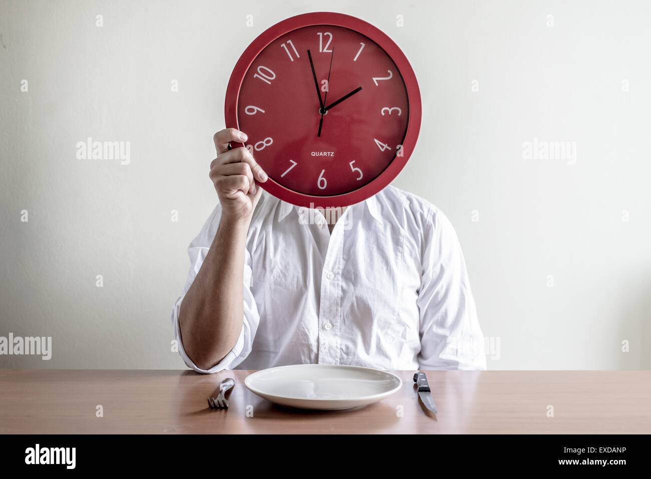 young stylish man with white shirt holding red clock behind a table ...