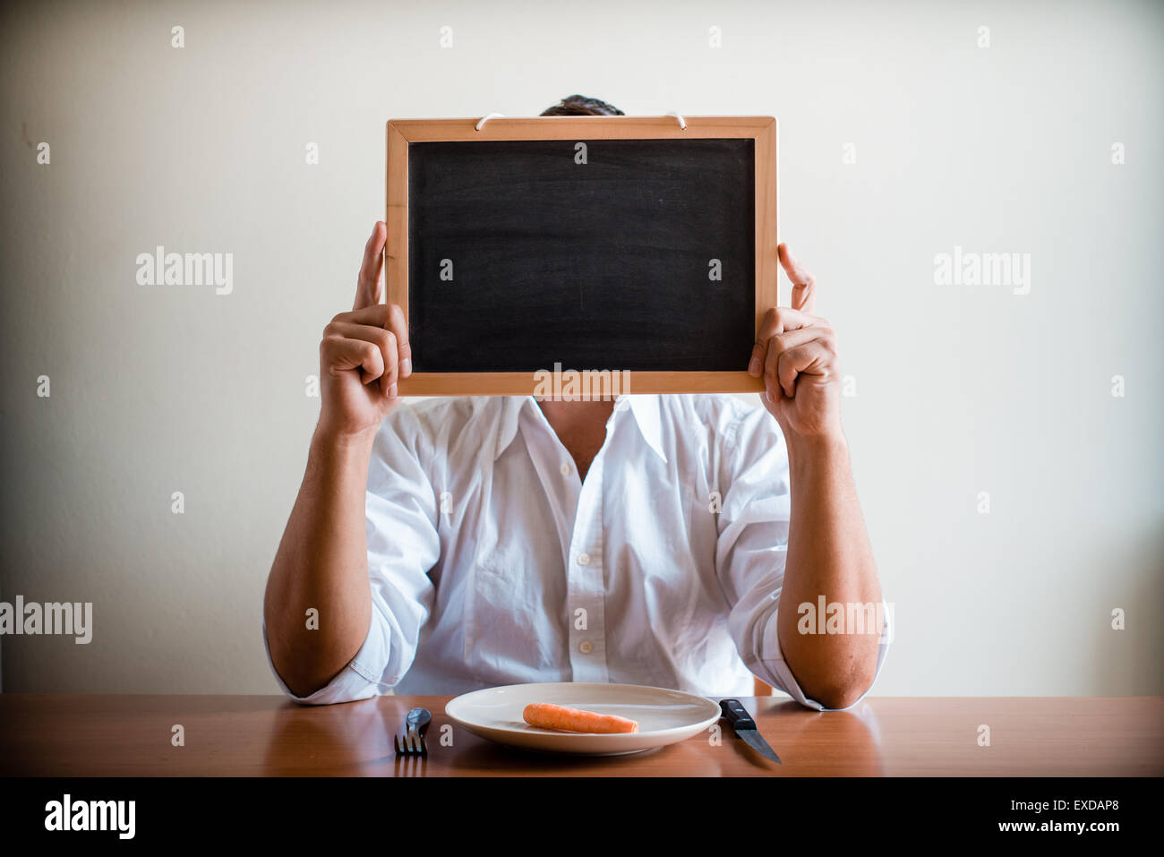 young stylish man with white shirt holding blackboard behind a table ...