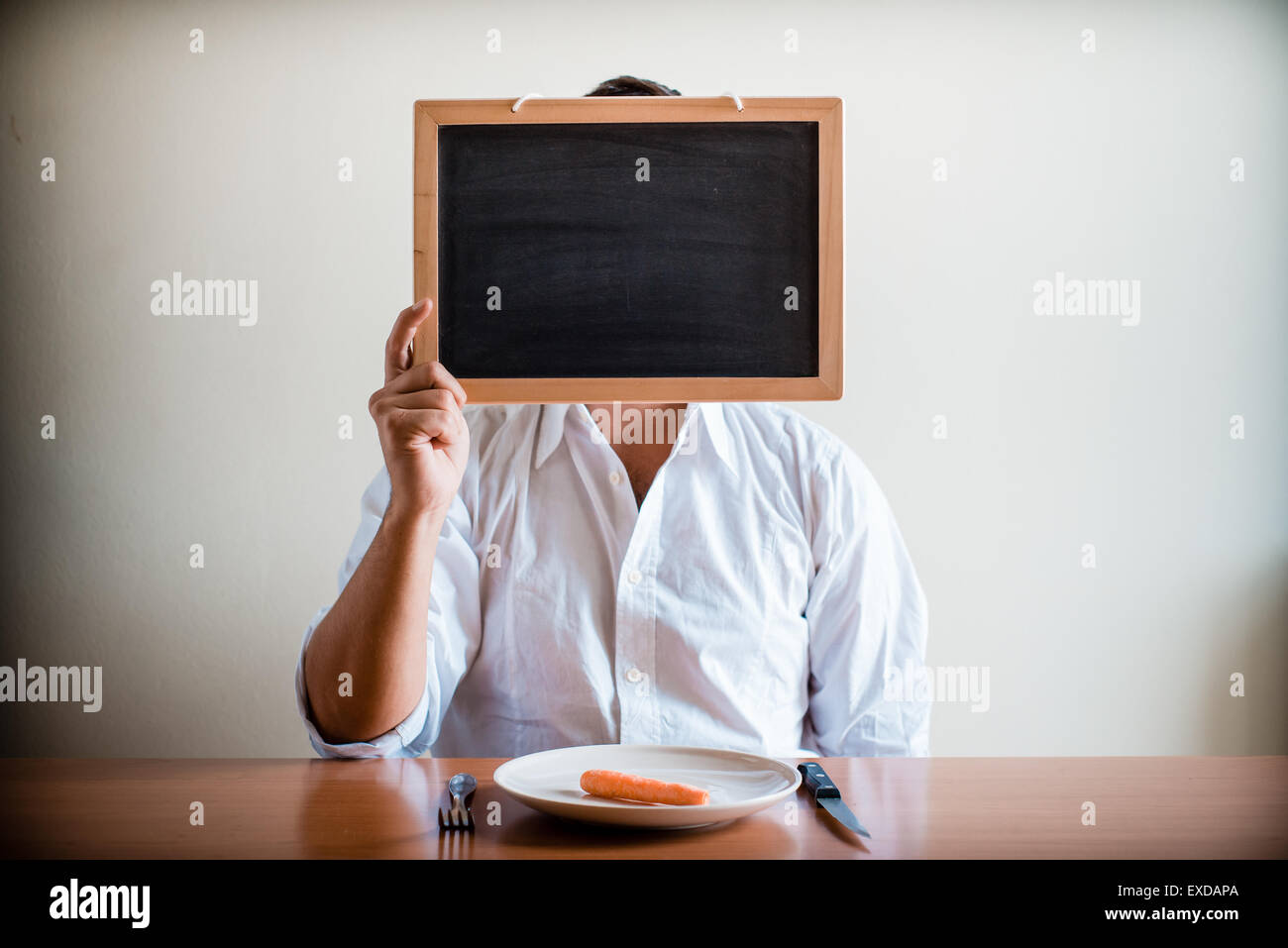 young stylish man with white shirt holding blackboard behind a table ...