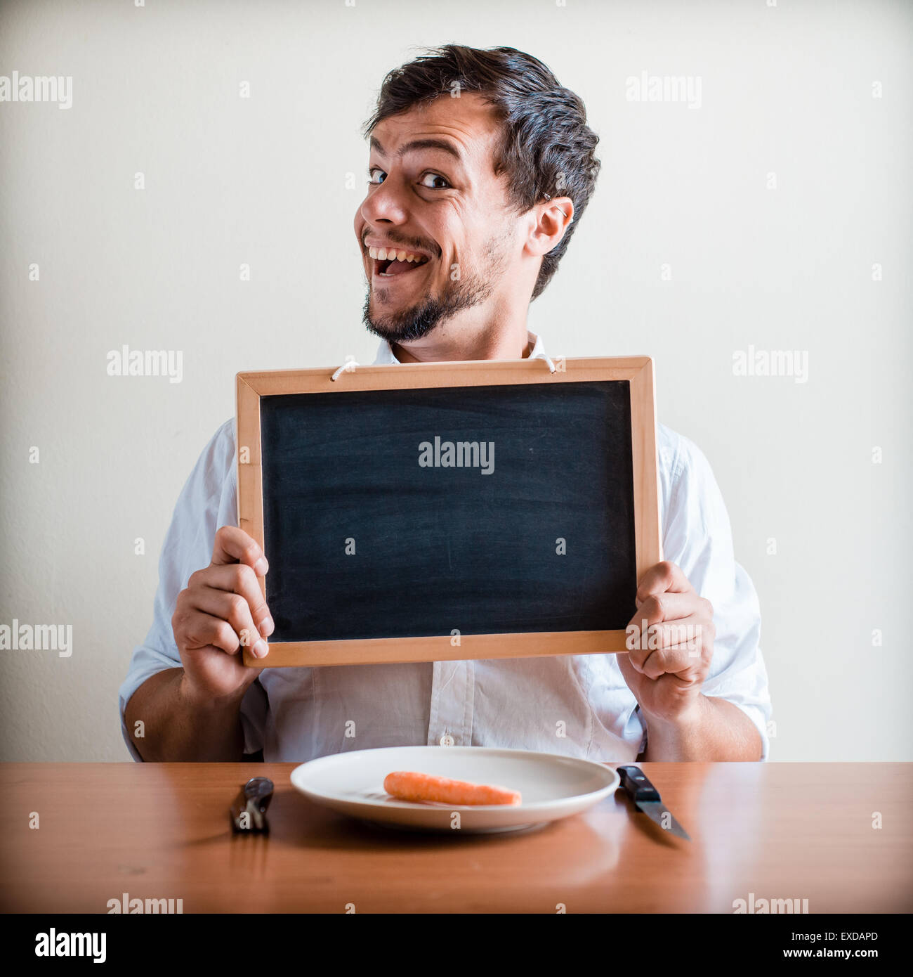 young stylish man with white shirt holding blackboard behind a table ...