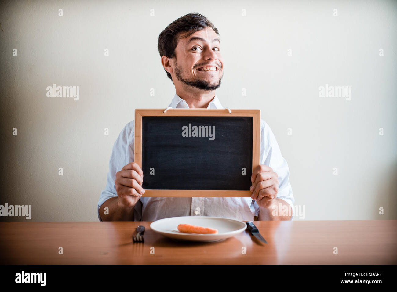 young stylish man with white shirt holding blackboard behind a table ...