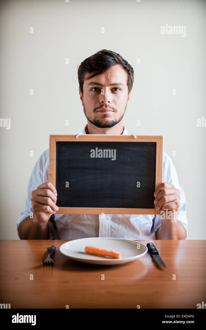 young stylish man with white shirt holding blackboard behind a table ...