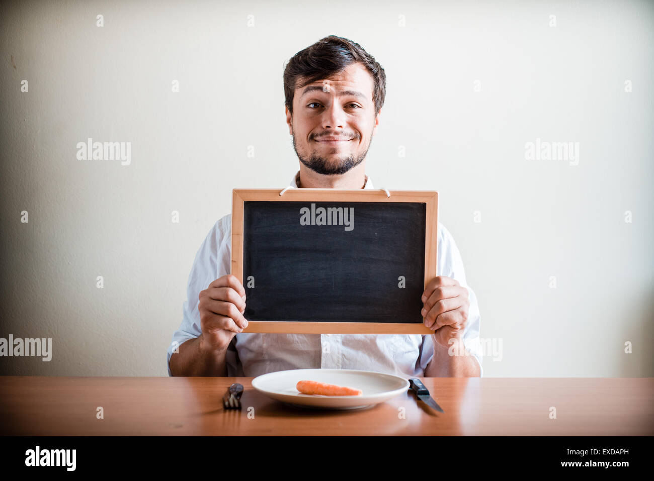 young stylish man with white shirt holding blackboard behind a table ...