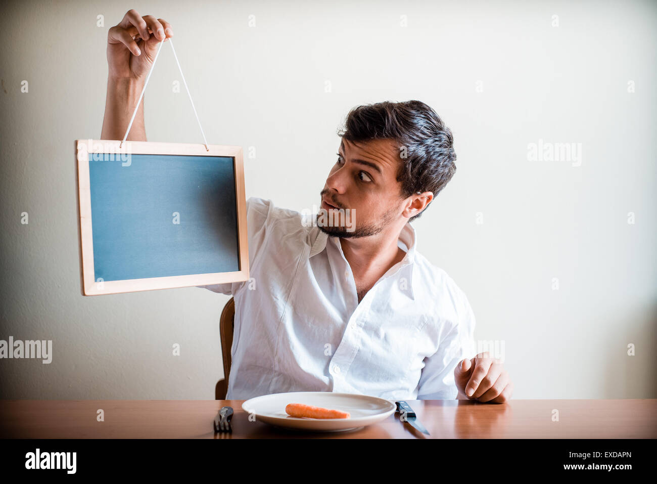 young stylish man with white shirt holding blackboard behind a table ...