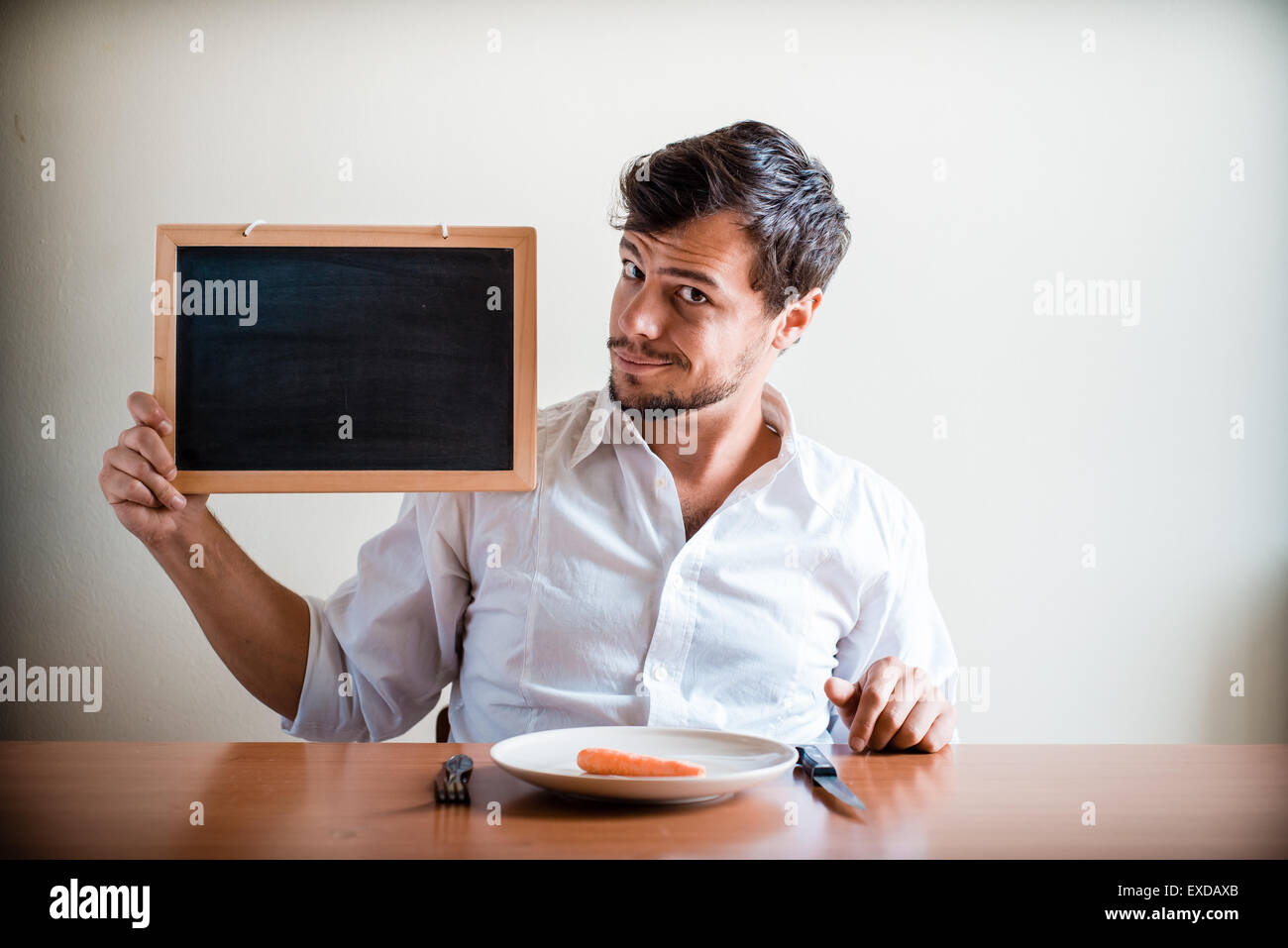 young stylish man with white shirt holding blackboard behind a table ...