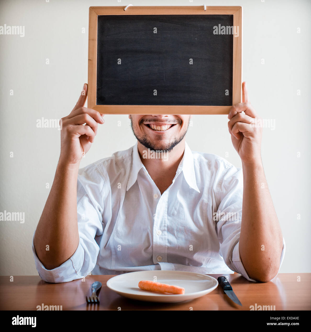 young stylish man with white shirt holding blackboard behind a table ...