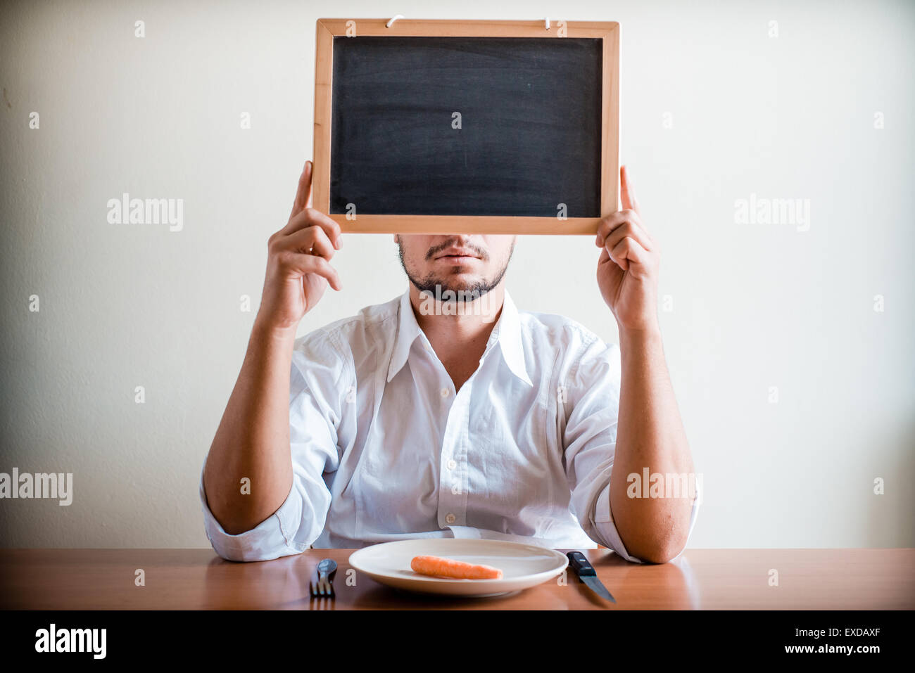 young stylish man with white shirt holding blackboard behind a table ...