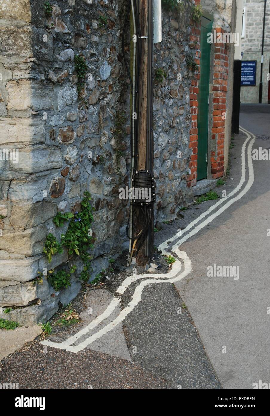 Wavy double yellow lines go around a telegraph pole on a narrow street ...