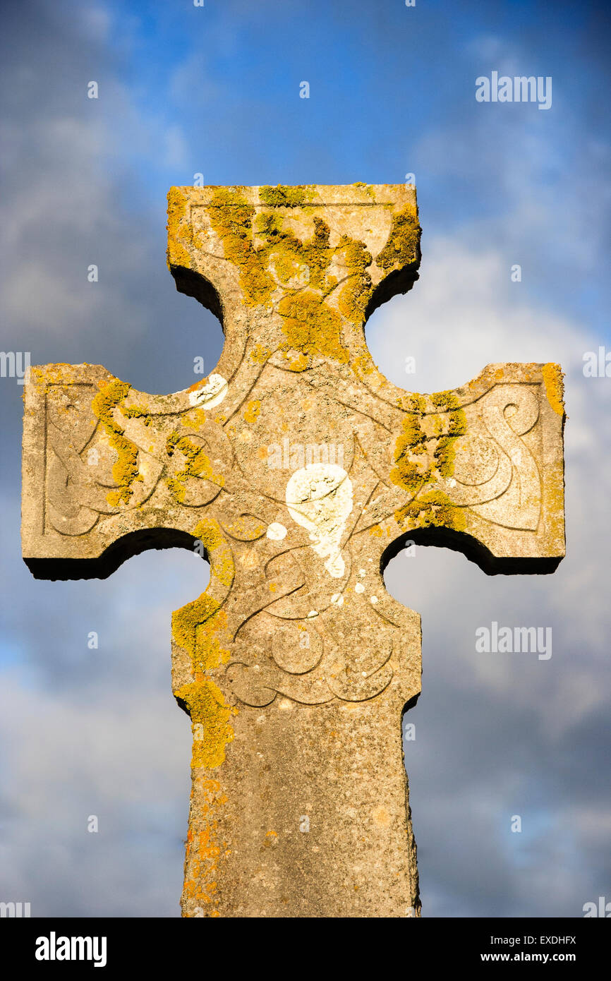 Sunlit old stone Christian cross in the churchyard at the English ...