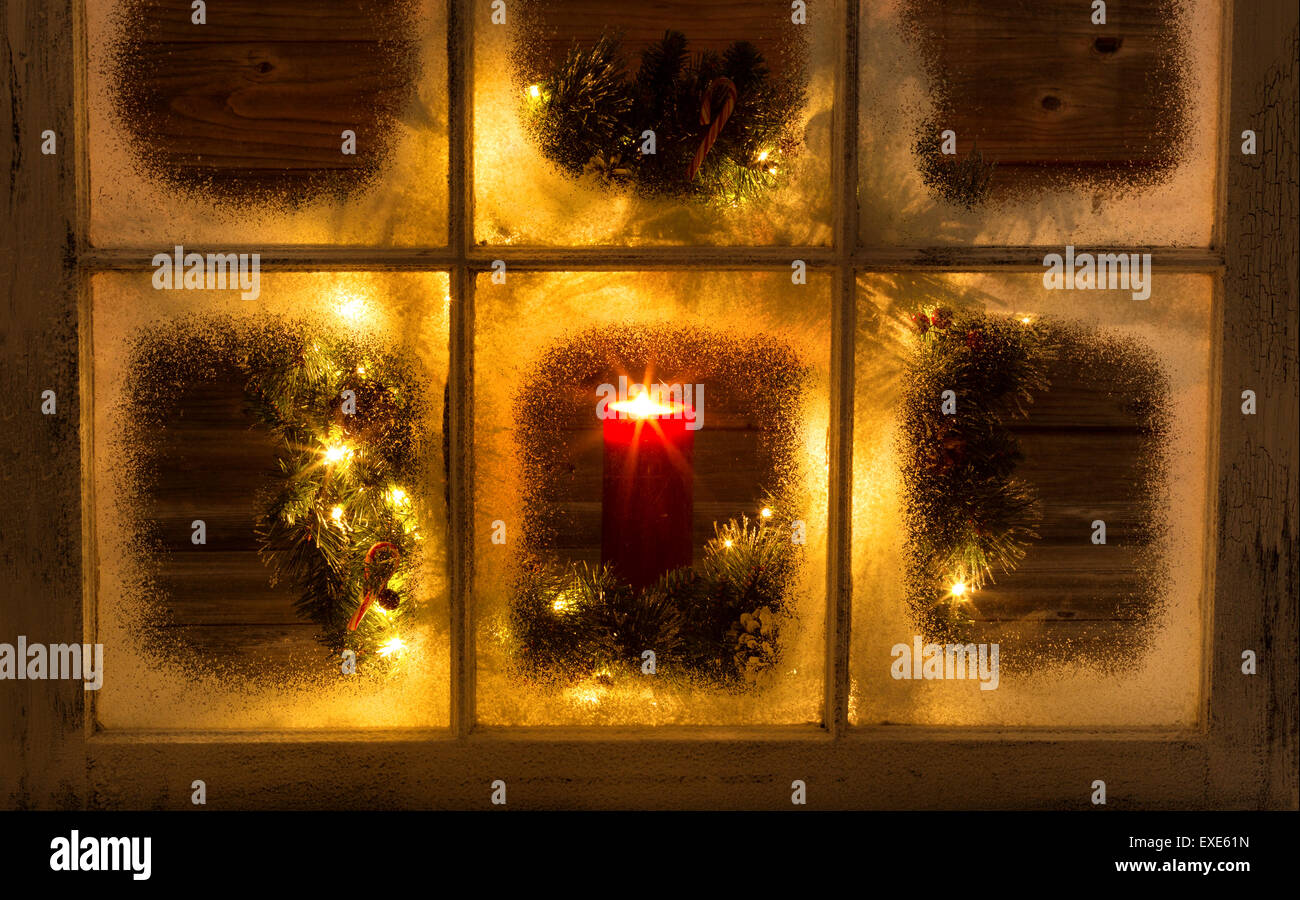 Snow covered window with glowing candle and decorative Christmas wreath ...