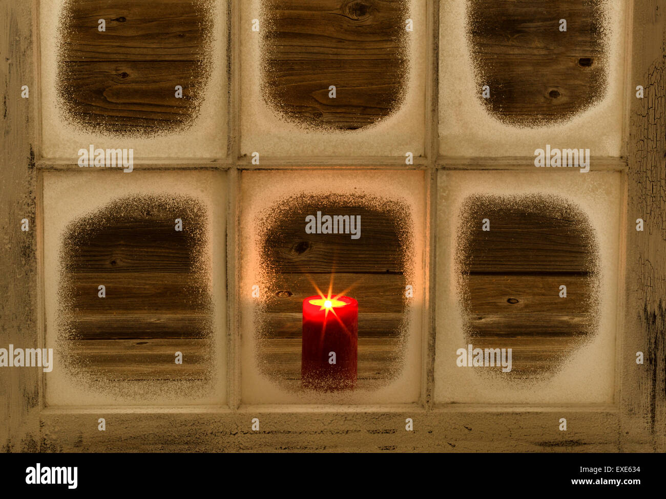 Snow covered window and glowing red candle on rustic wood background ...