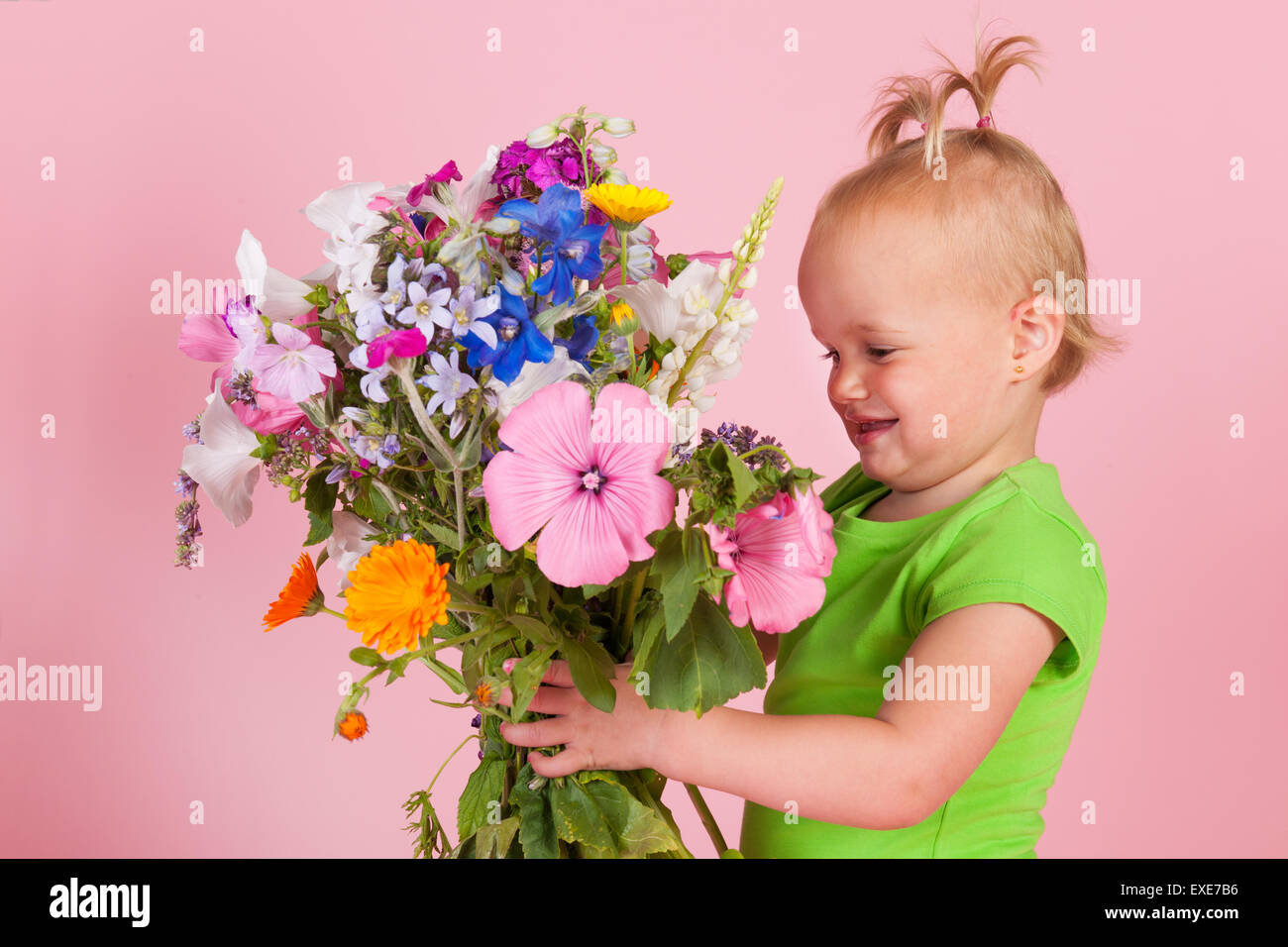Portrait toddler girl with bouquet garden flowers on pink background ...