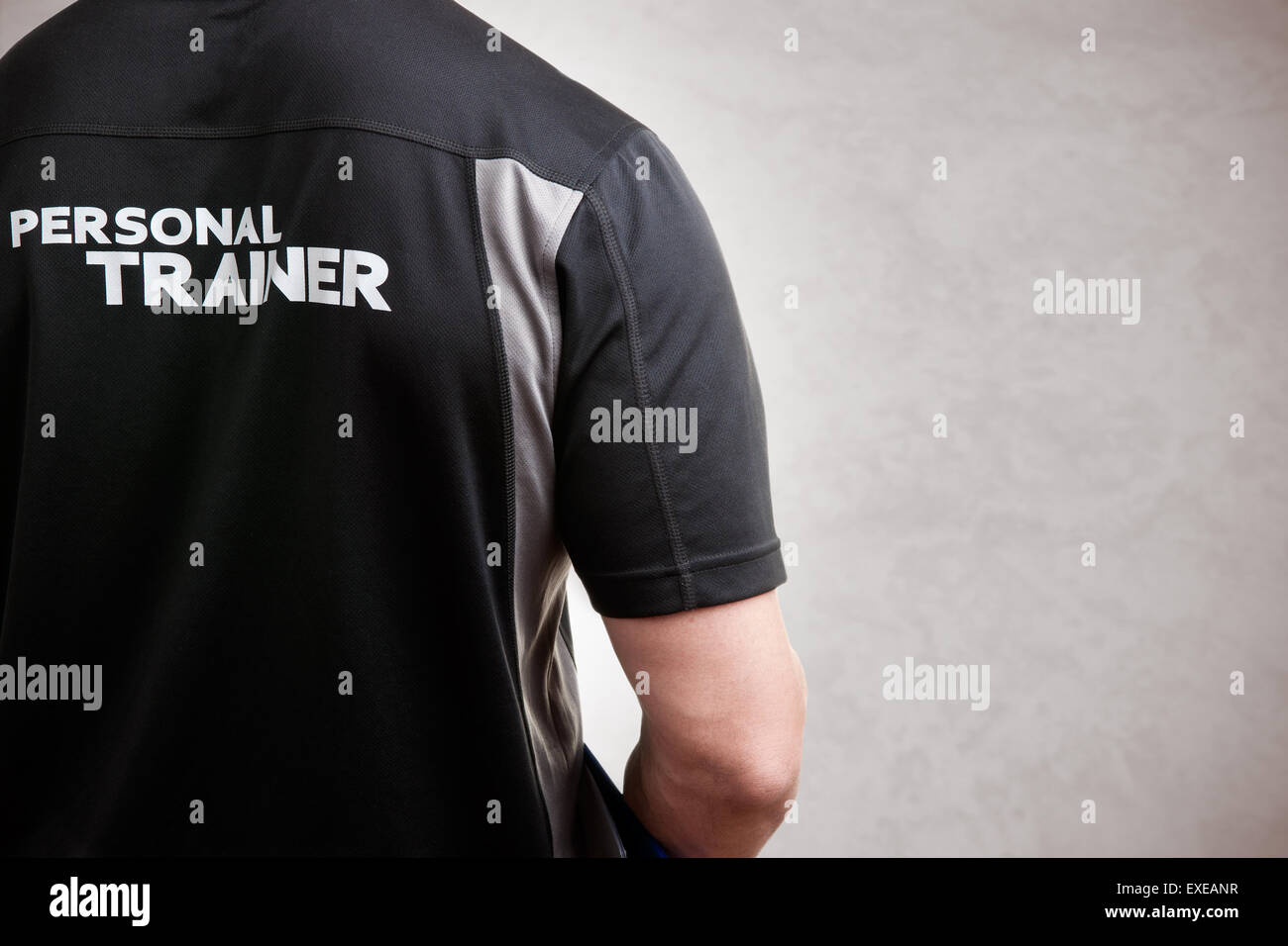 Personal Trainer, with his back facing the camera, in a grey background ...