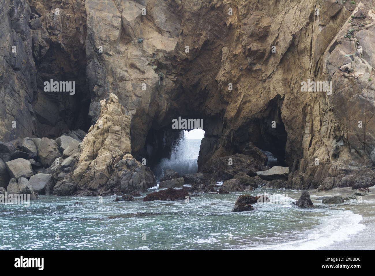 close up of a large rock with a natural tunnel and waves flowing thru ...
