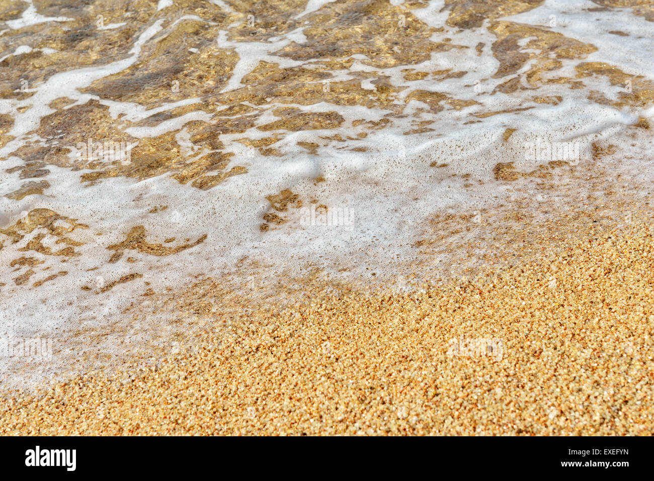 Wet beach sand with semi-transparent grains and sea waves in sunny day ...