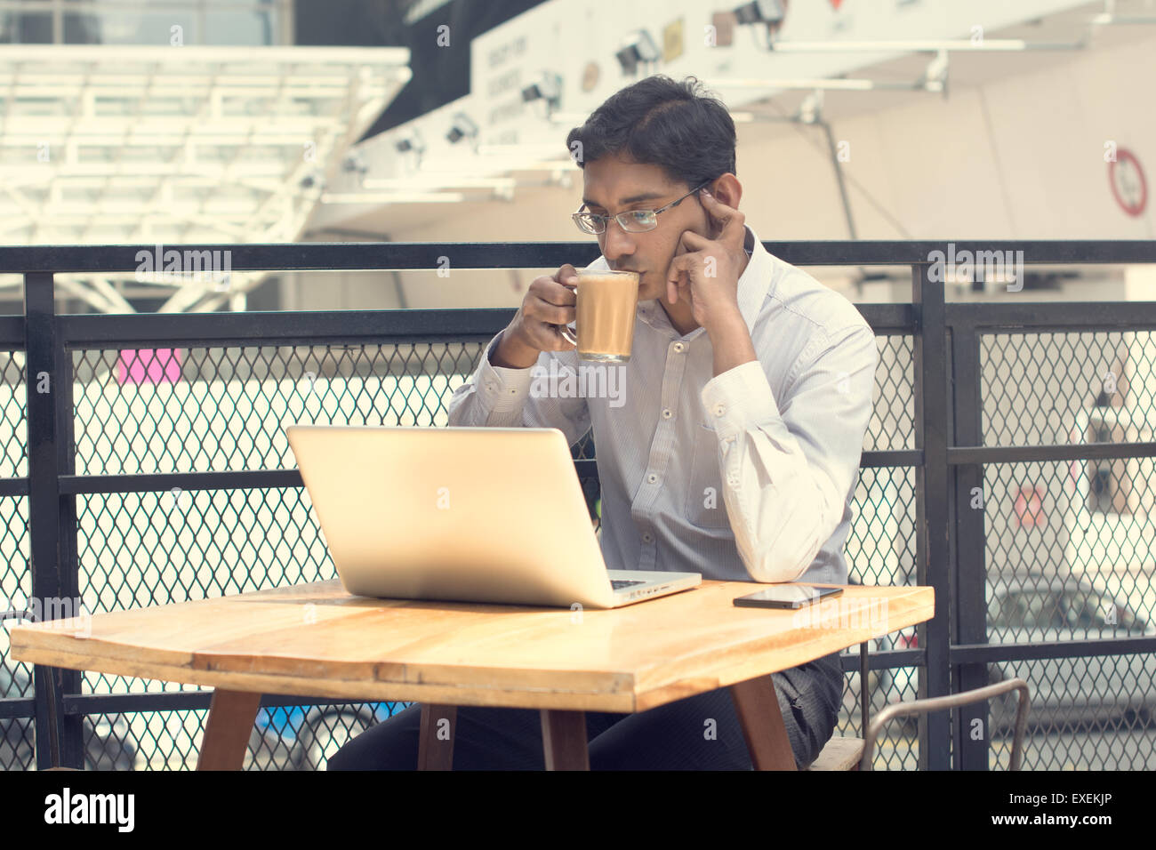 Asian Indian businessman using laptop computer while drinking a cup hot ...