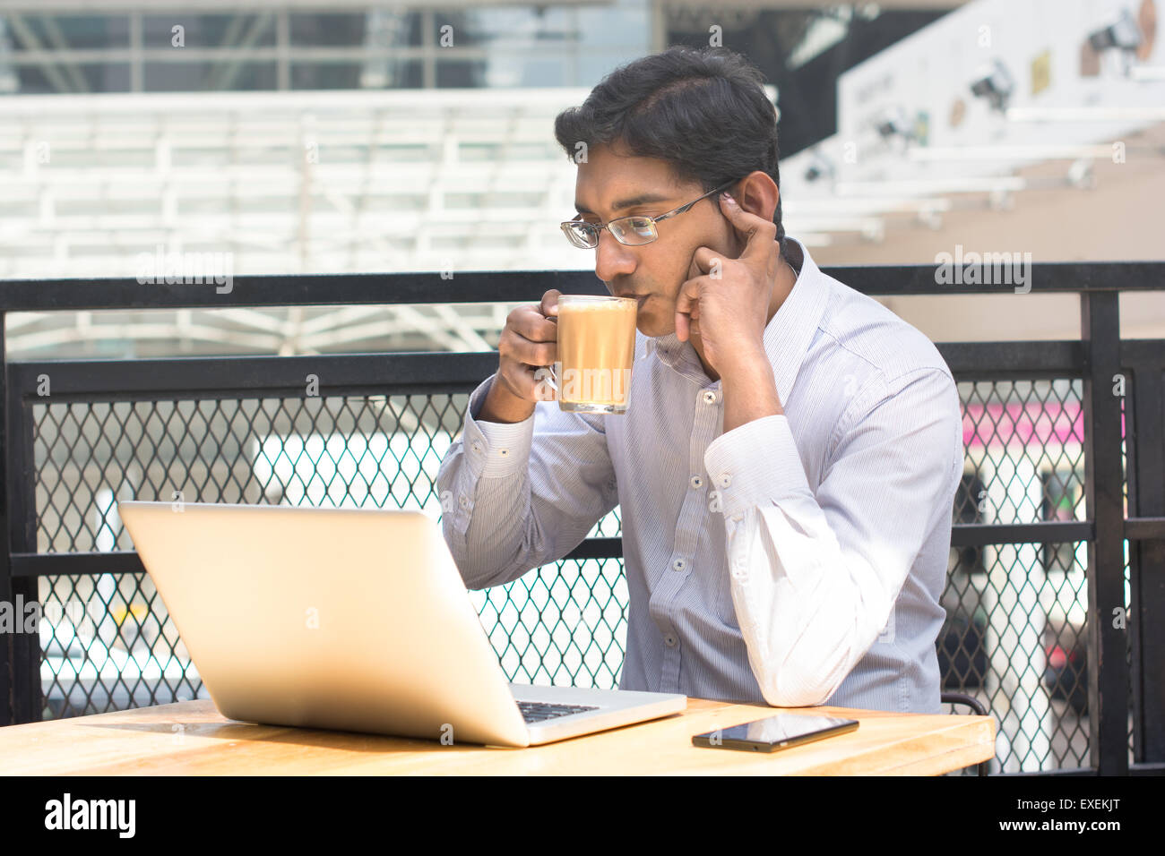Asian Indian businessman using laptop computer while drinking a cup hot ...
