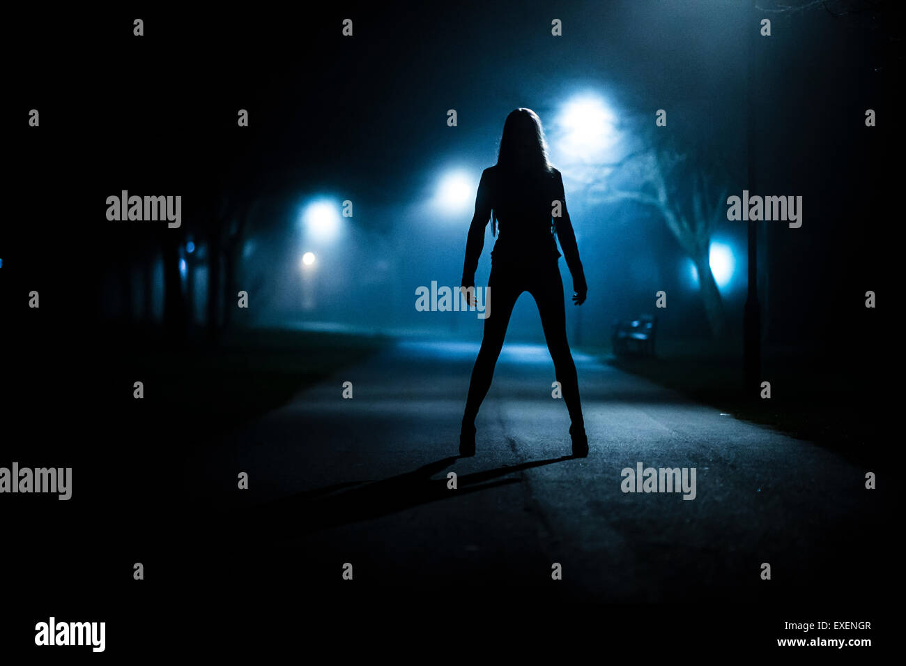 A young slim woman dressed in black alone on a misty foggy night ...
