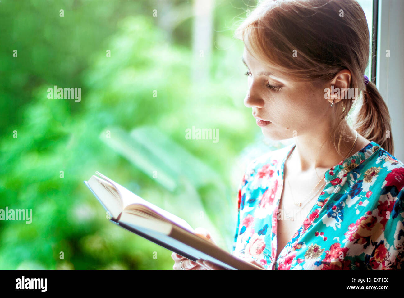 Young pretty girl reading a book near the window Stock Photo - Alamy