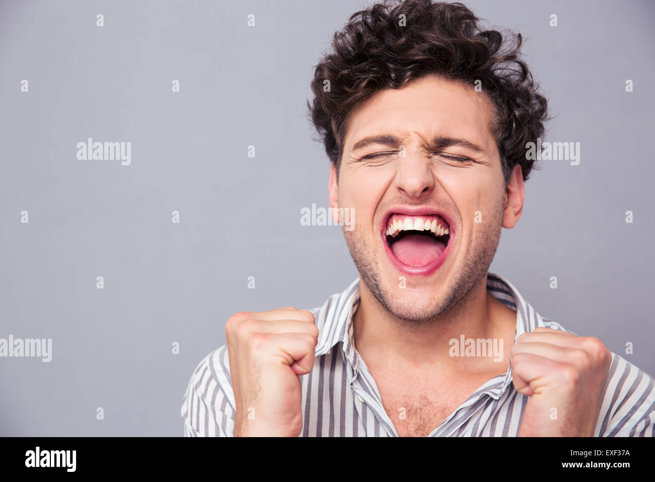 Portrait of a happy man celebrating his success over gray background ...