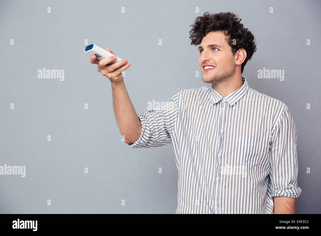 Happy young man holding TV remote over gray background Stock Photo - Alamy