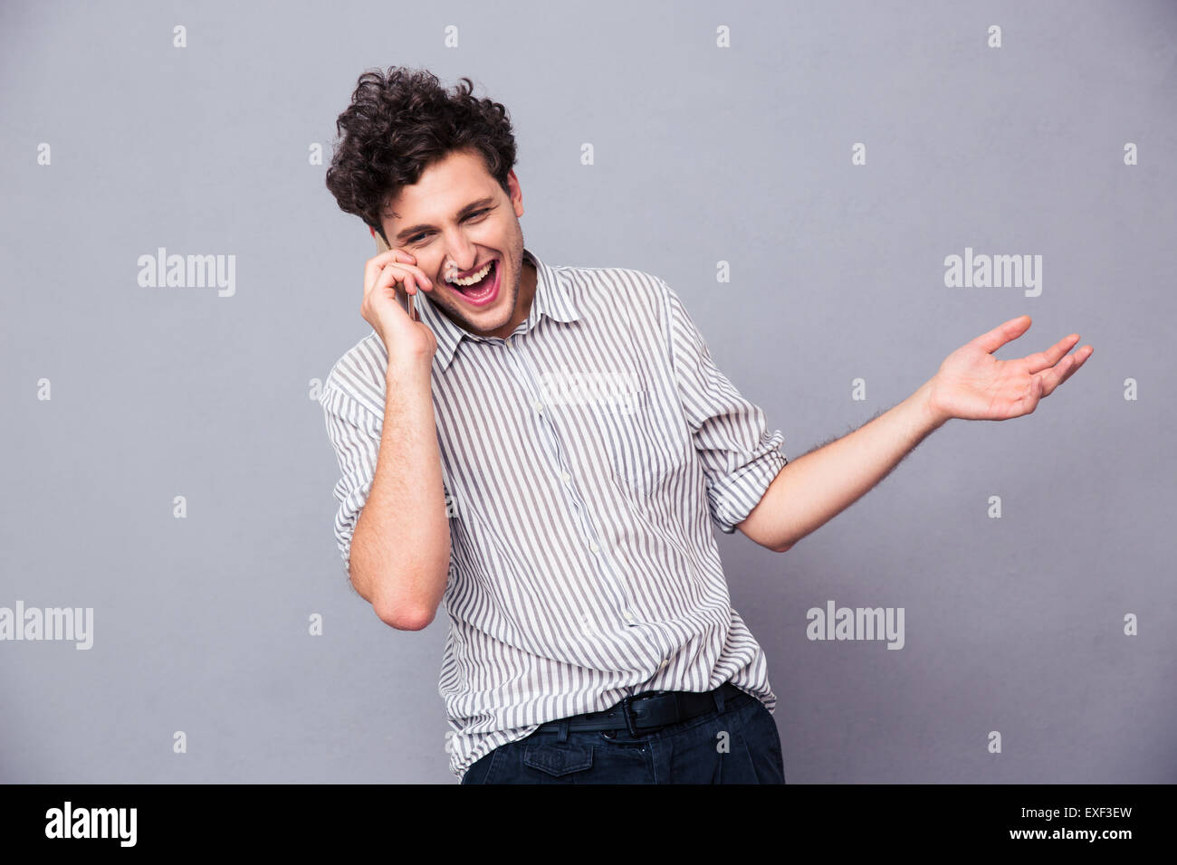 Cheerful young man talking on the phone over gray background Stock ...
