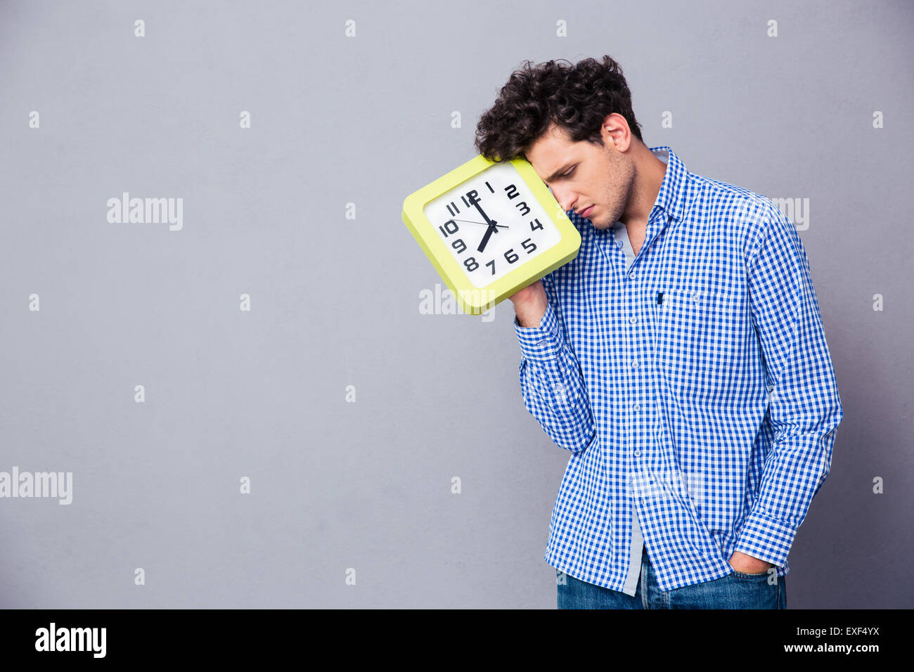 Tired man holding big clock over gray background Stock Photo - Alamy