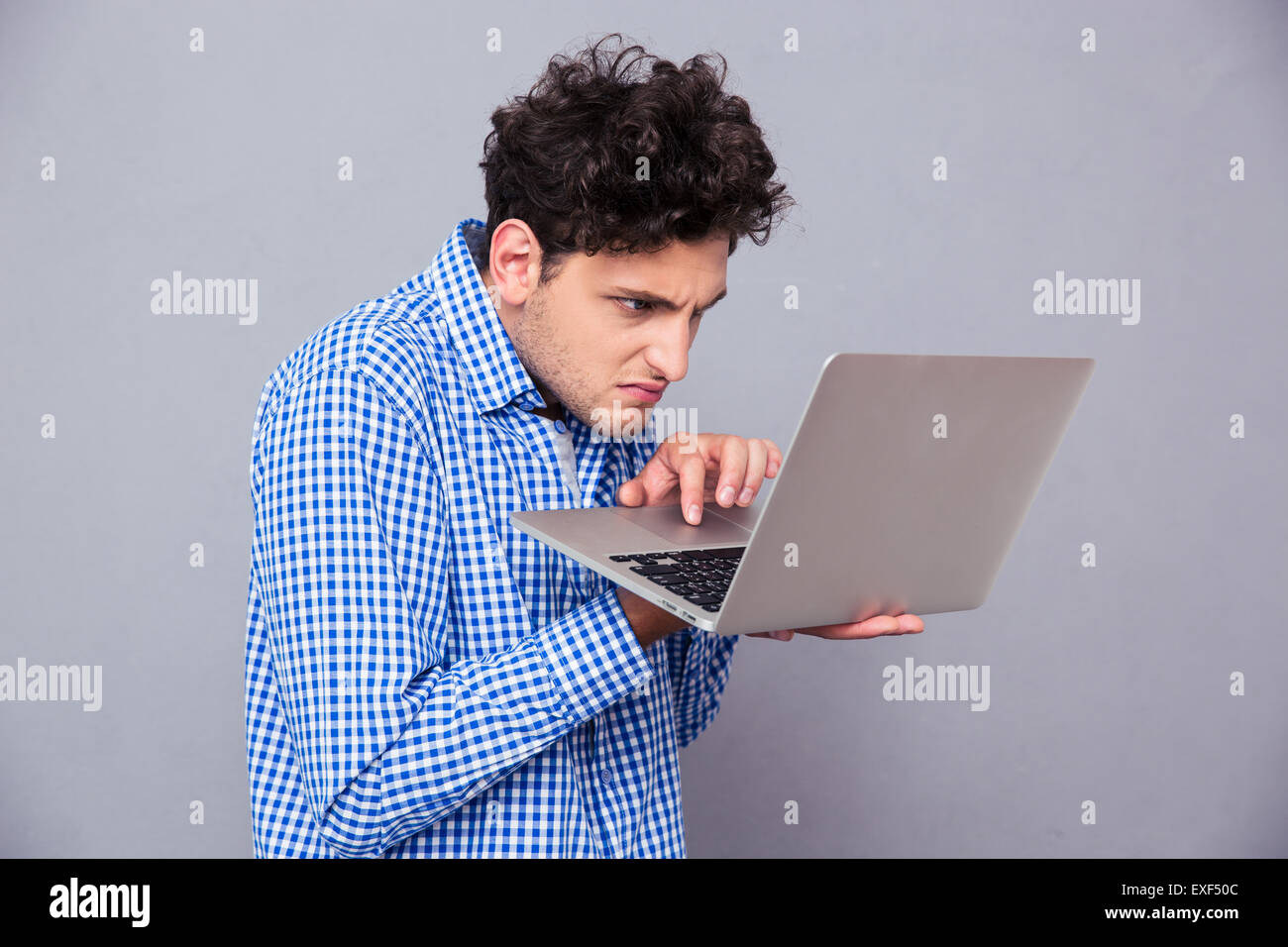 Angry man standing and using laptop over gray background Stock Photo ...